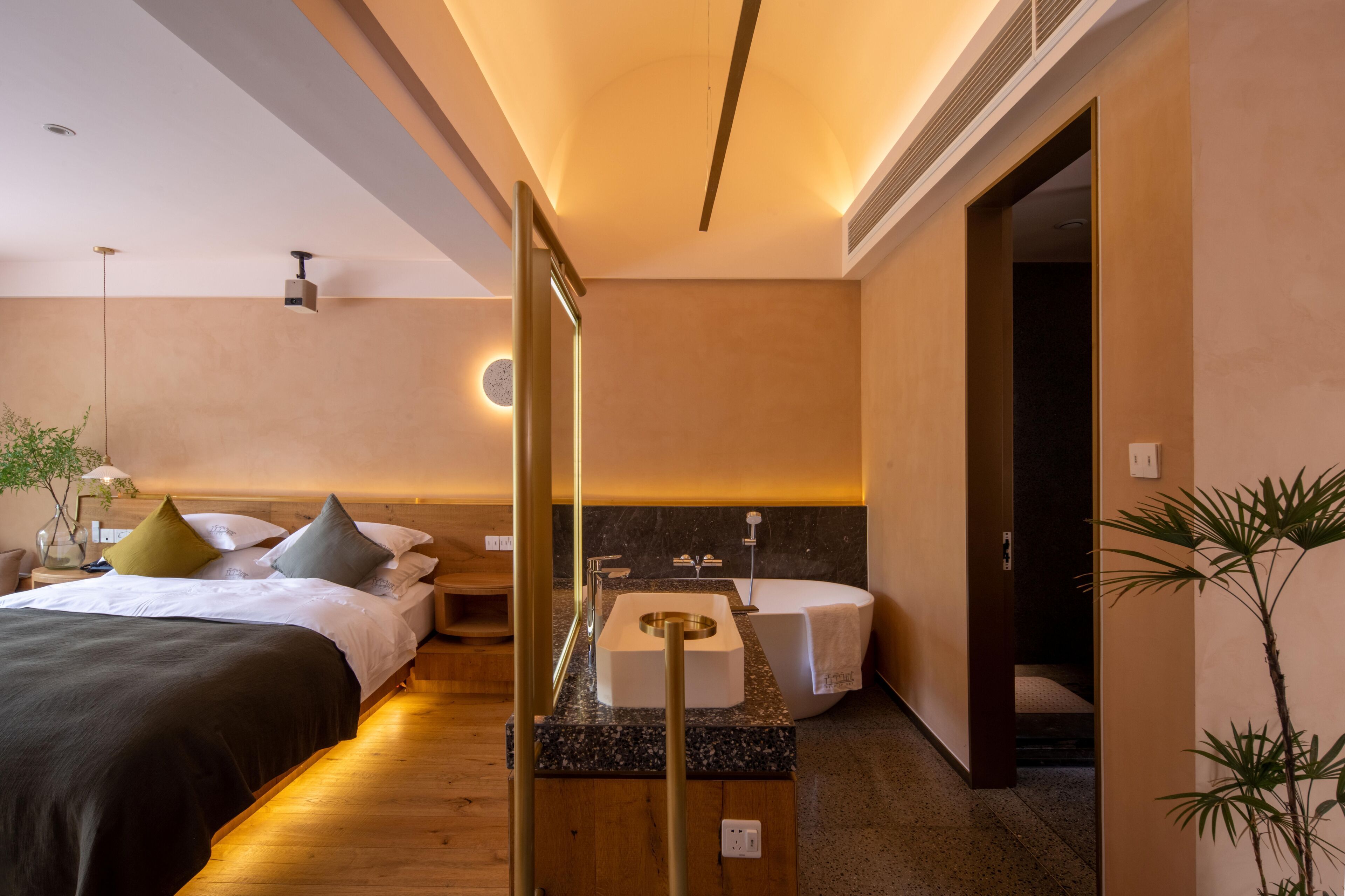 Quarto de hotel moderno com uma cama grande, banheiro com pia independente e piso de madeira.
