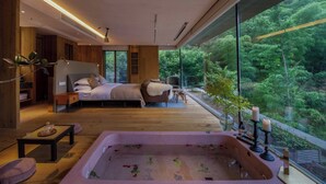 Quarto moderno com uma cama grande, um espaço para sentar com uma mesa e uma banheira com pétalas de rosa.