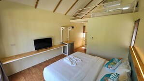 Quarto com cama, televisão em uma estante, uma pequena mesa de trabalho e uma janela.