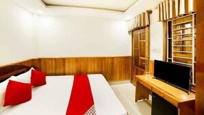 Quarto de hotel com cama, escrivaninha, televisão e guarda-roupa.