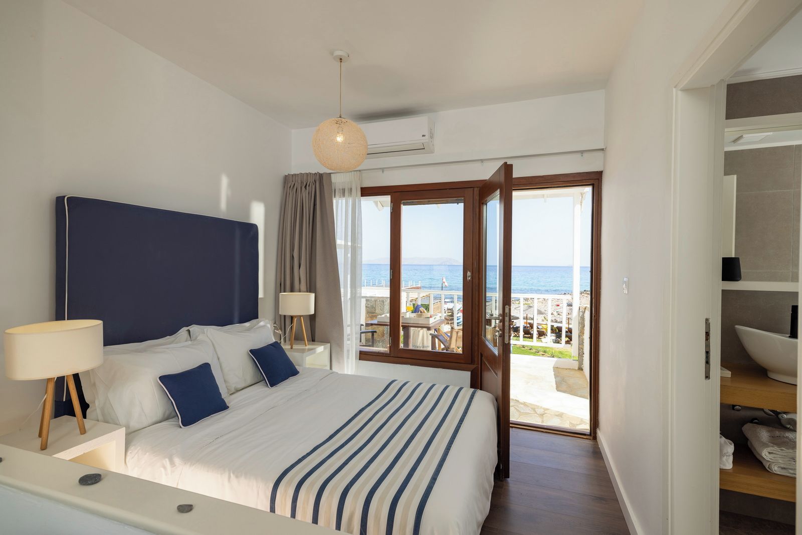 Quarto de hotel com uma cama grande, vista para o mar, varanda e banheiro.