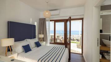 Quarto de hotel com uma cama grande, vista para o mar, varanda e banheiro.