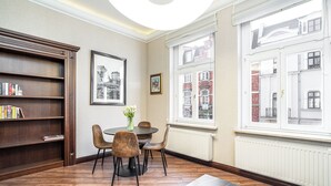Uma sala de jantar com uma mesa redonda, quatro cadeiras, uma estante e uma janela com vista para edifícios.