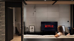 Uma sala de estar moderna com uma grande televisão de tela plana exibindo o logotipo da Netflix, um sofá e uma mesa de centro.