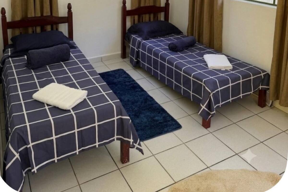 Quarto com duas camas, um tapete azul e cortinas nas janelas.