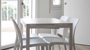 Mesa de jantar branca com quatro cadeiras em um quarto com porta de vidro deslizante que dá para uma varanda.