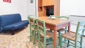 Um quarto com uma mesa de jantar de madeira, cadeiras verdes, um sofá azul e uma televisão em um suporte.