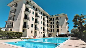 Um hotel com vários andares, piscina, varandas e um céu azul claro.