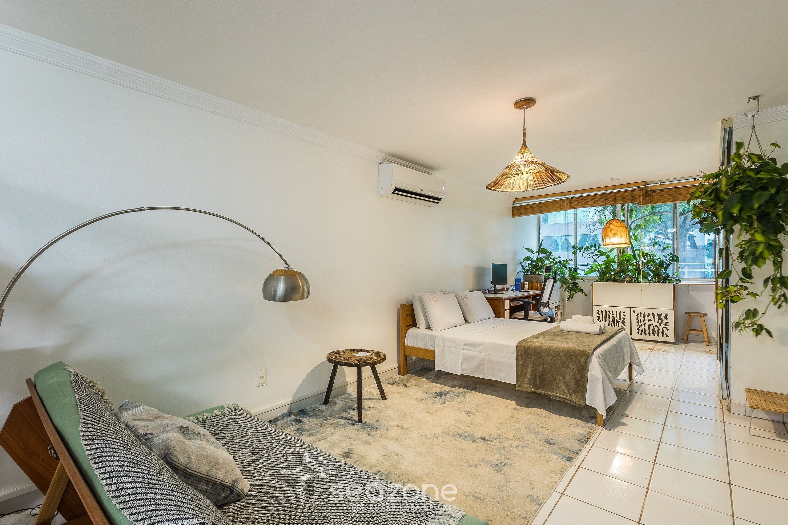 Quarto moderno com cama, mesa de cabeceira e escrivaninha. Há uma janela com vista para o exterior.