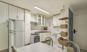 Cozinha com armários brancos, geladeira, fogão e mesa de jantar com cadeiras.