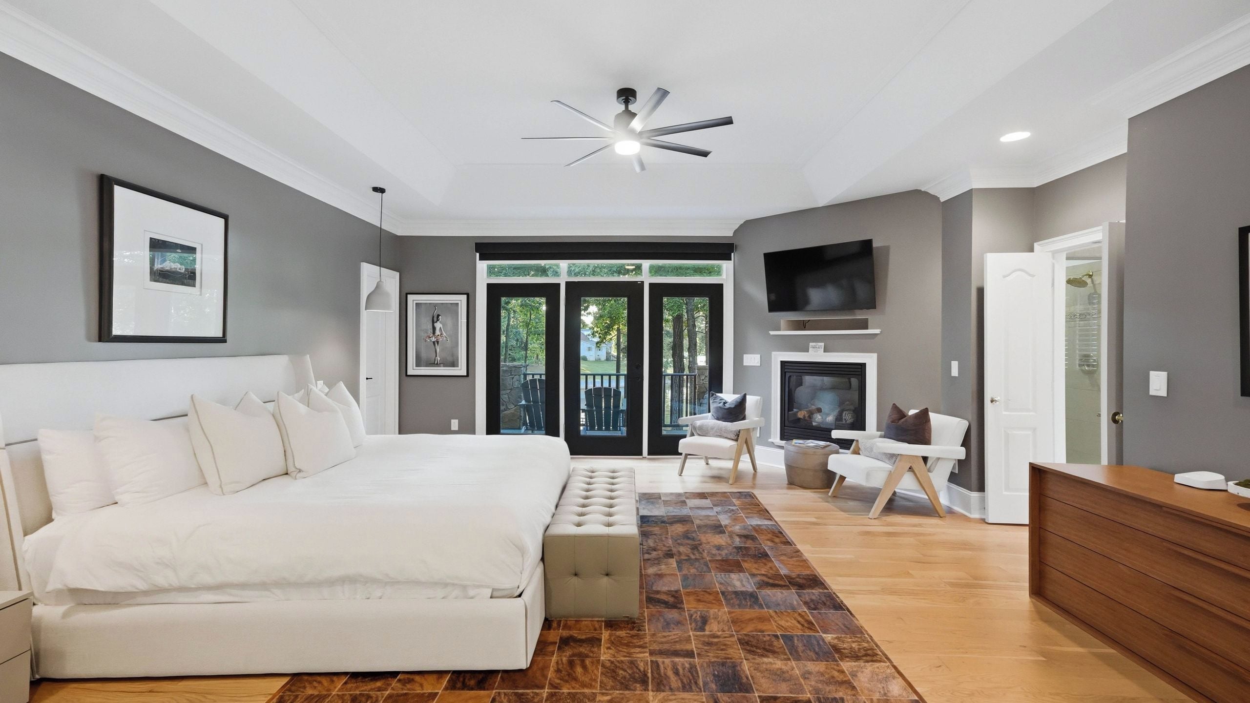 Quarto moderno com uma cama grande, ventilador de teto, lareira e vista para o exterior.
