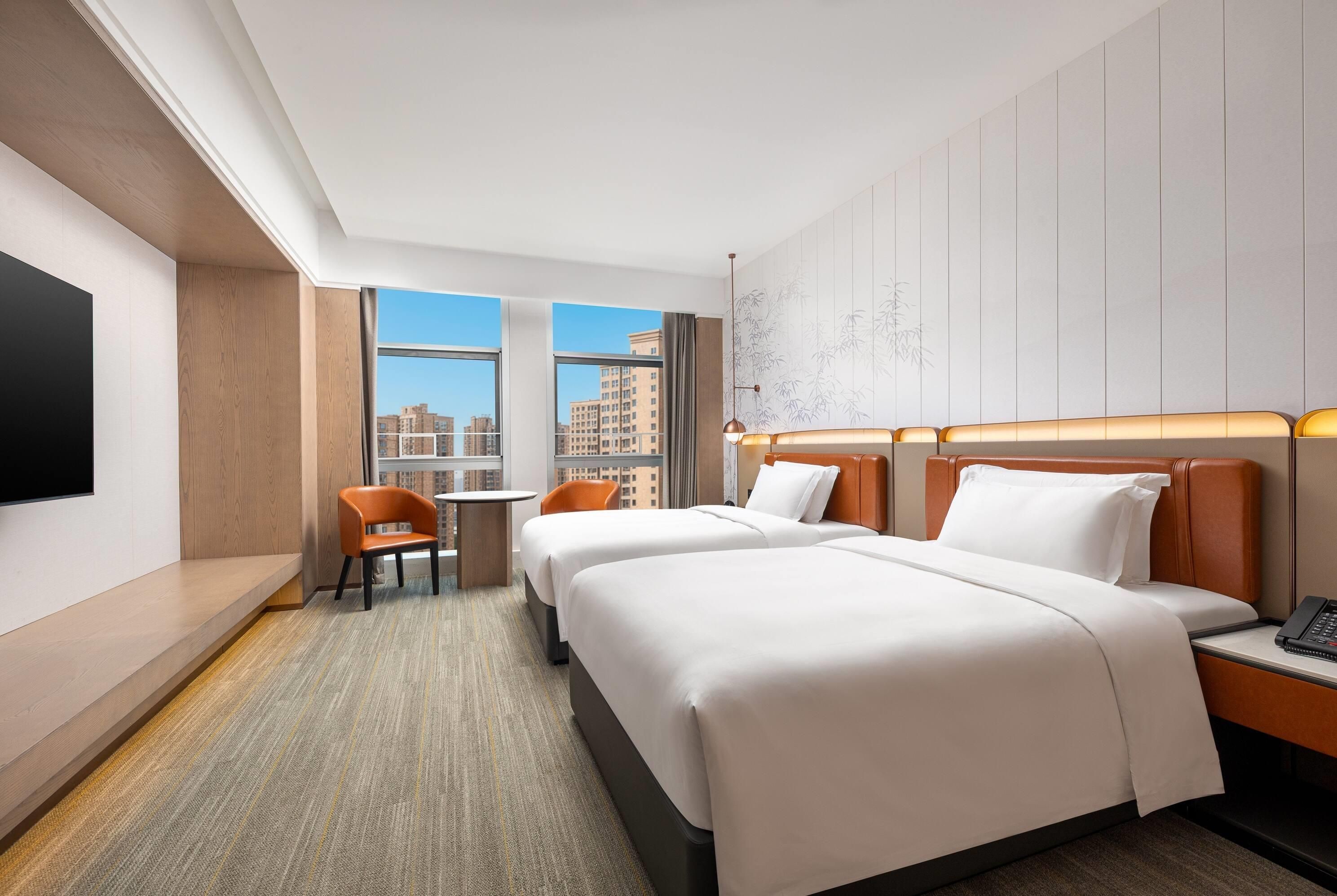 Quarto de hotel com duas camas, uma mesa, uma cadeira, televisão e vista para a cidade.