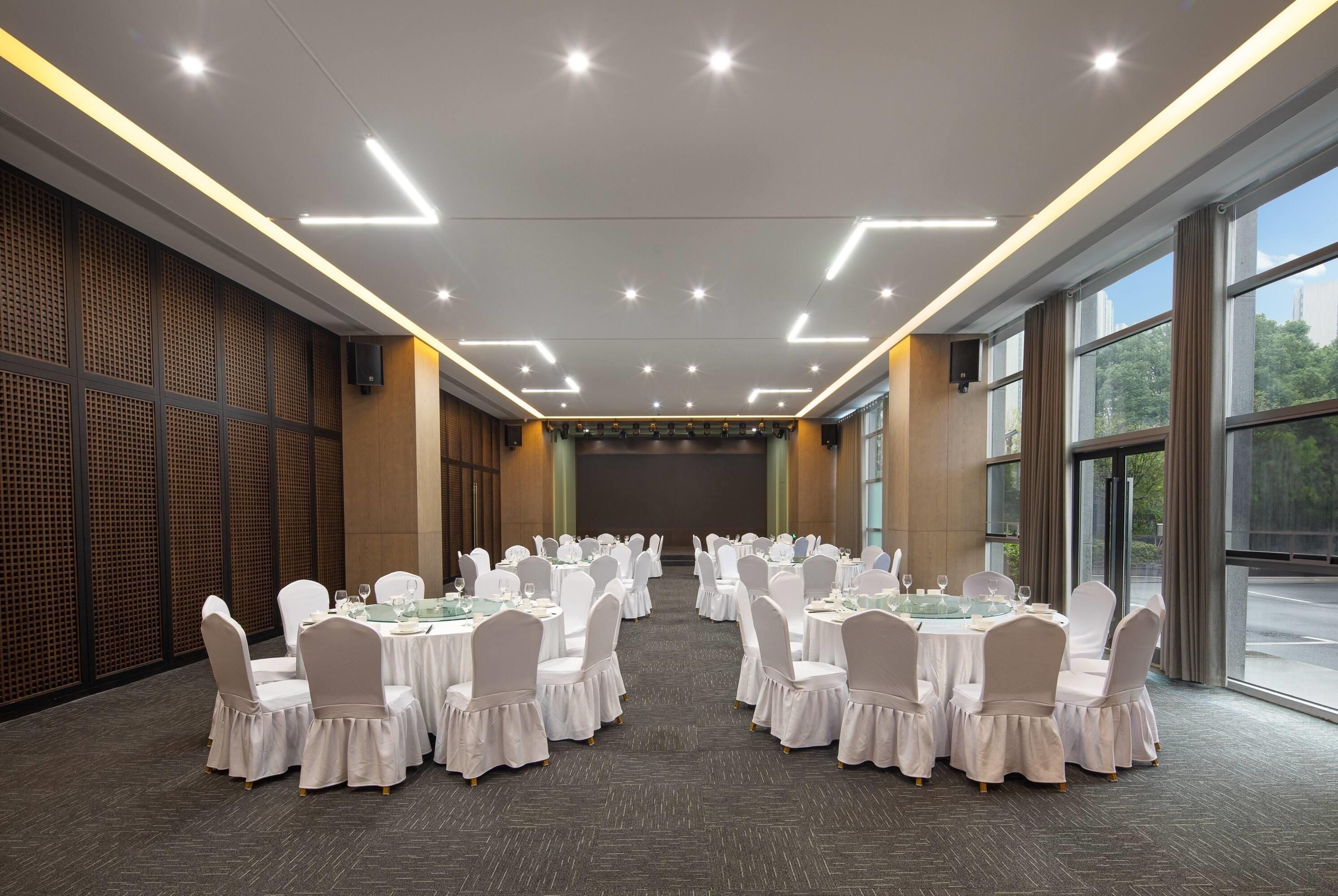 Uma sala de conferências com mesas redondas, cadeiras brancas e um design de teto moderno.