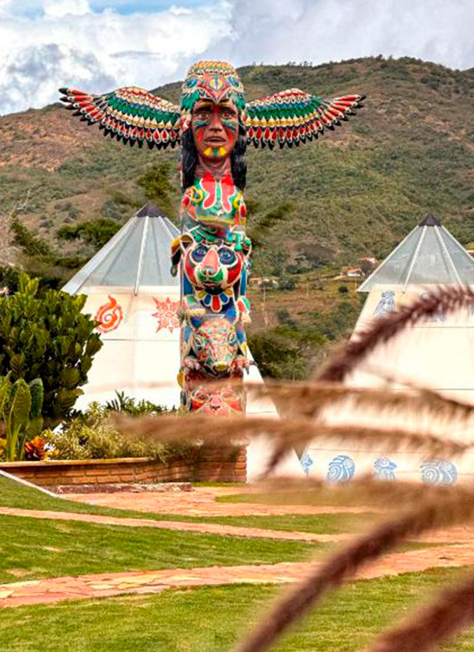 Uma estátua colorida com asas e um cocar, ao fundo montanhas.