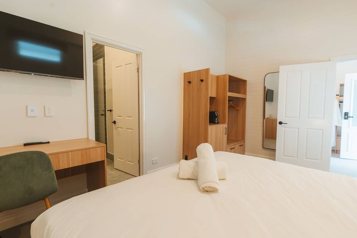 Quarto de hotel com cama, escrivaninha, cadeira, televisão e guarda-roupa.