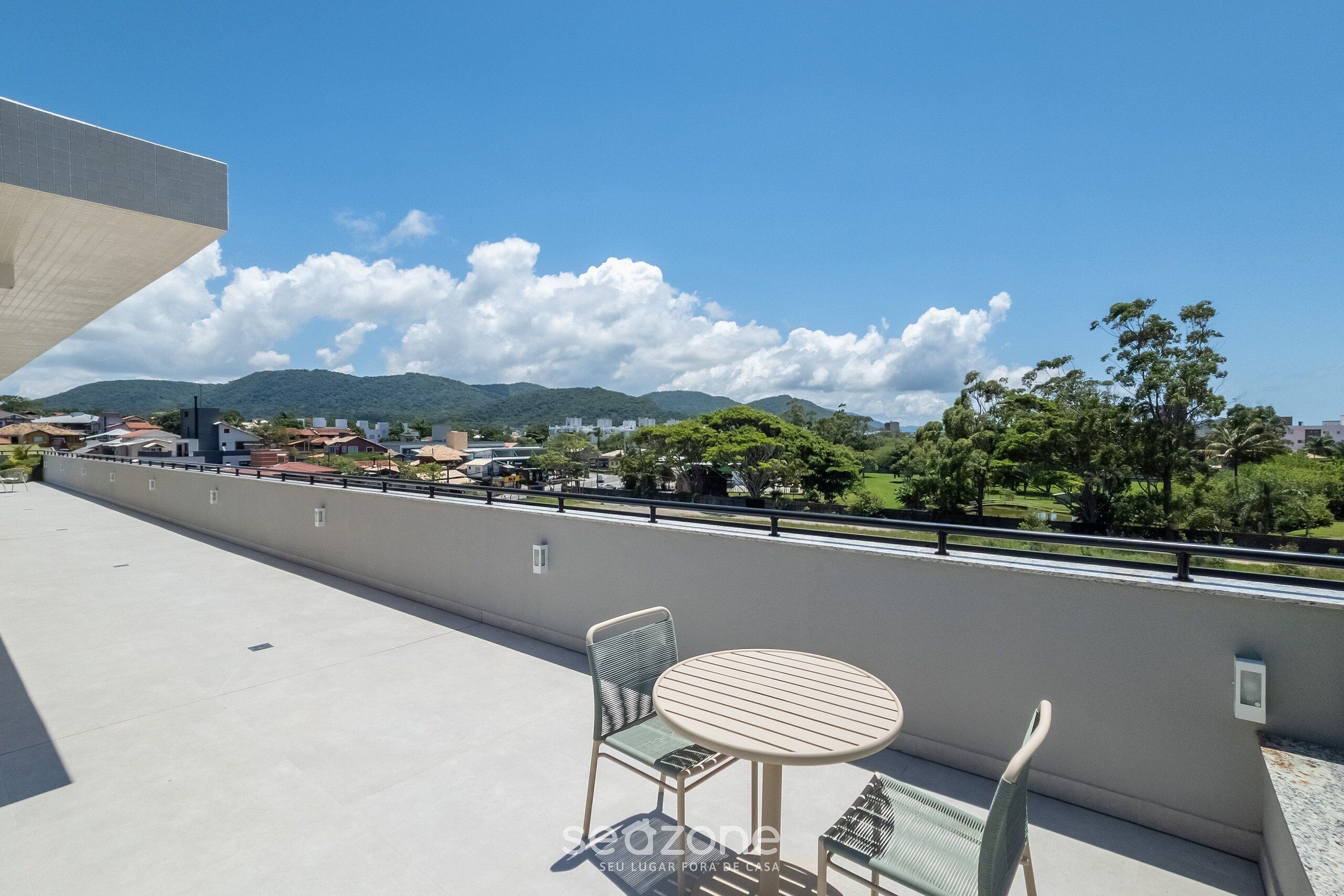 Terraço no telhado com mesa e cadeiras, com vista para a paisagem urbana e montanhas.