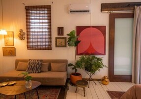 Uma sala de estar com sofá, mesa de centro, planta em vaso e uma grande pintura abstrata na parede.