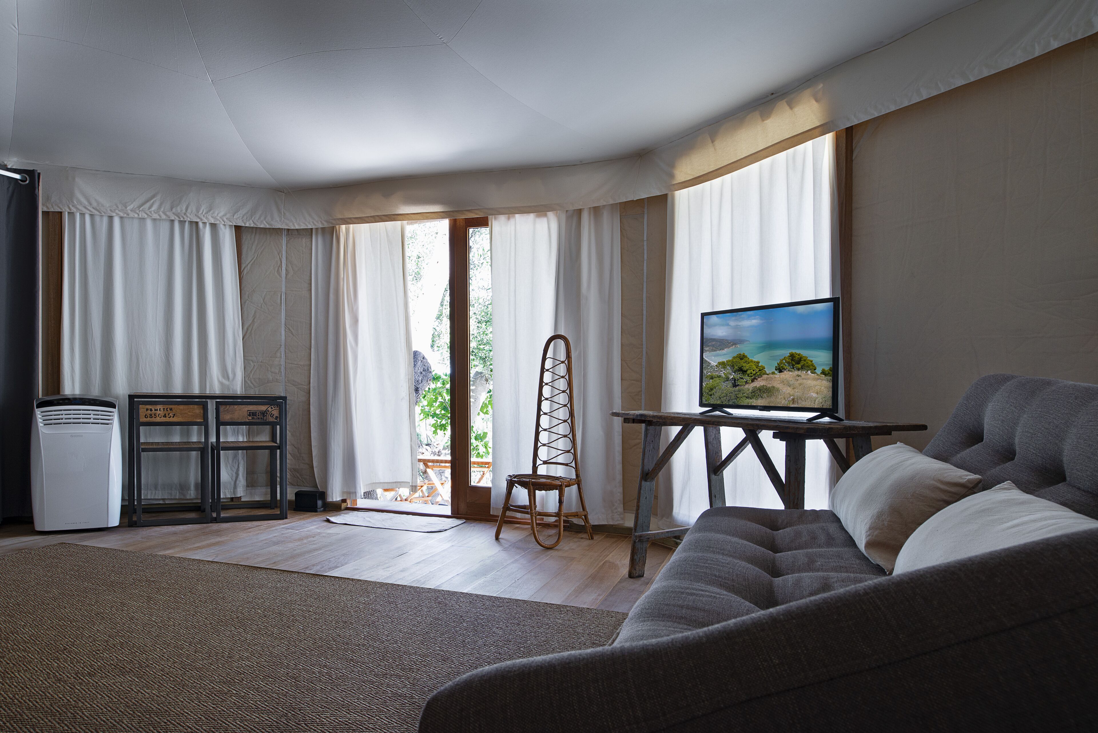 Uma sala de estar com sofá, televisão e janela com cortinas.