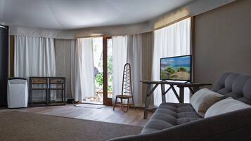 Uma sala de estar com sofá, televisão e janela com cortinas.