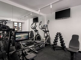 Ginásio com equipamentos de cardio, halteres e uma tela de televisão.