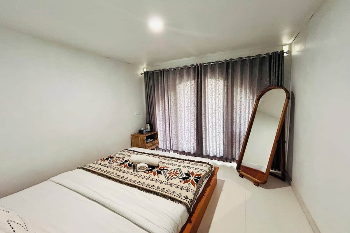 Quarto com cama, mesa de cabeceira, espelho e janela com cortinas.
