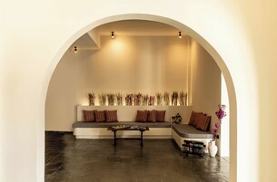 Uma sala de estar moderna com uma parede branca curva, um sofá com almofadas estampadas, uma mesa de centro e um vaso com flores.