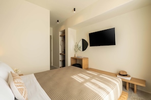 Quarto moderno com cama grande, um banco de madeira, televisão na parede e um guarda-roupa com espelho.