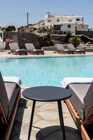 Uma área de piscina com espreguiçadeiras e uma pequena mesa, rodeada por muros de pedra e edifícios ao fundo.