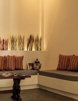 Um recanto acolhedor com um banco estofado, almofadas estampadas, um vaso decorativo e um livro sobre uma mesa pequena.