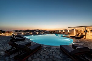 Piscina com espreguiçadeiras, deck de ladrilho e vista para a paisagem ao entardecer.