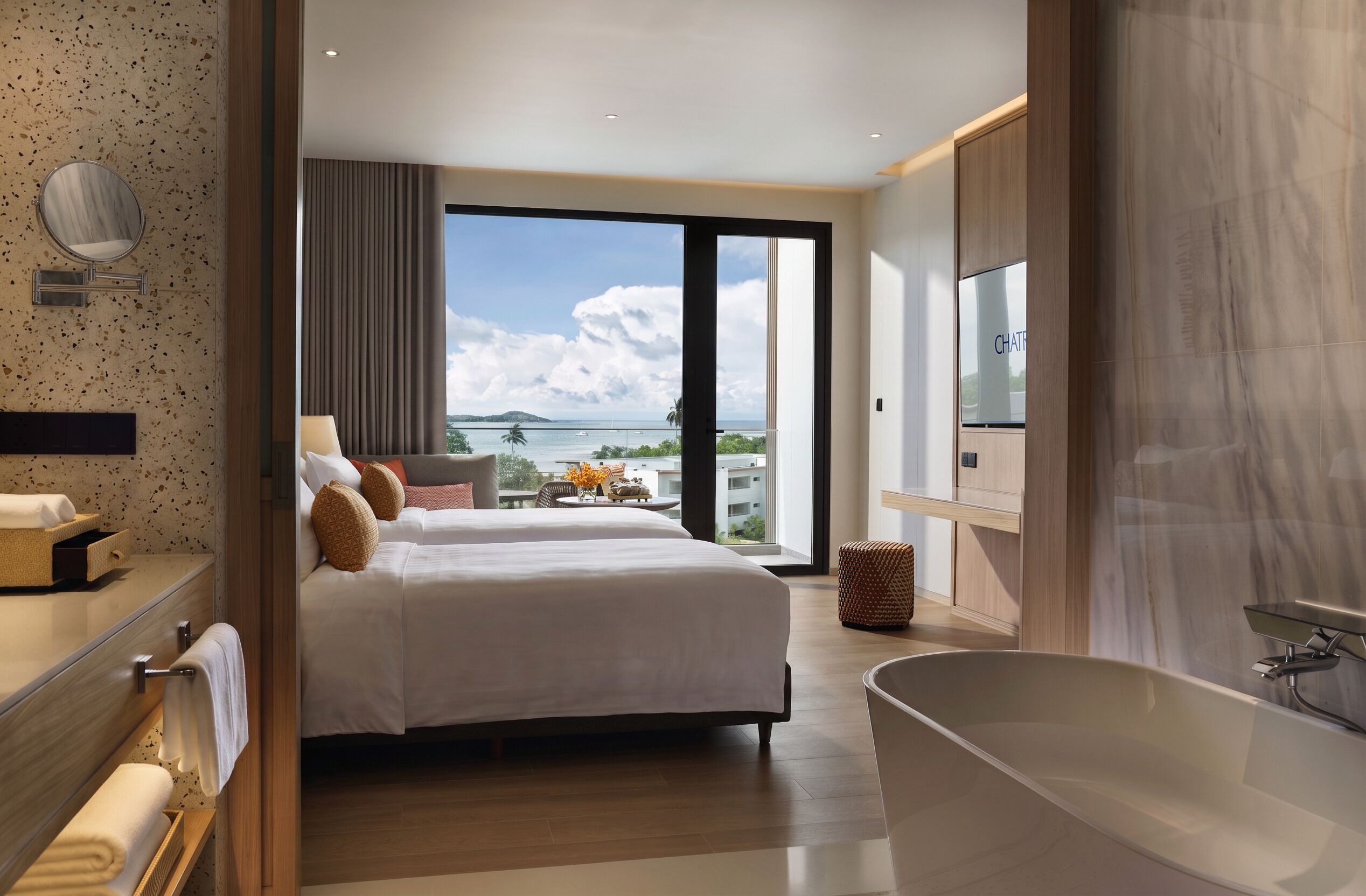 Quarto de hotel moderno com uma cama grande, uma banheira, uma TV e vista para o mar.
