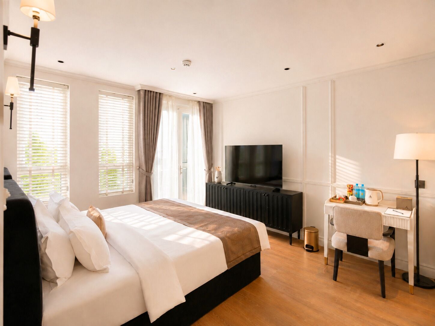Quarto de hotel com uma cama grande, televisão, escrivaninha e uma luminária.