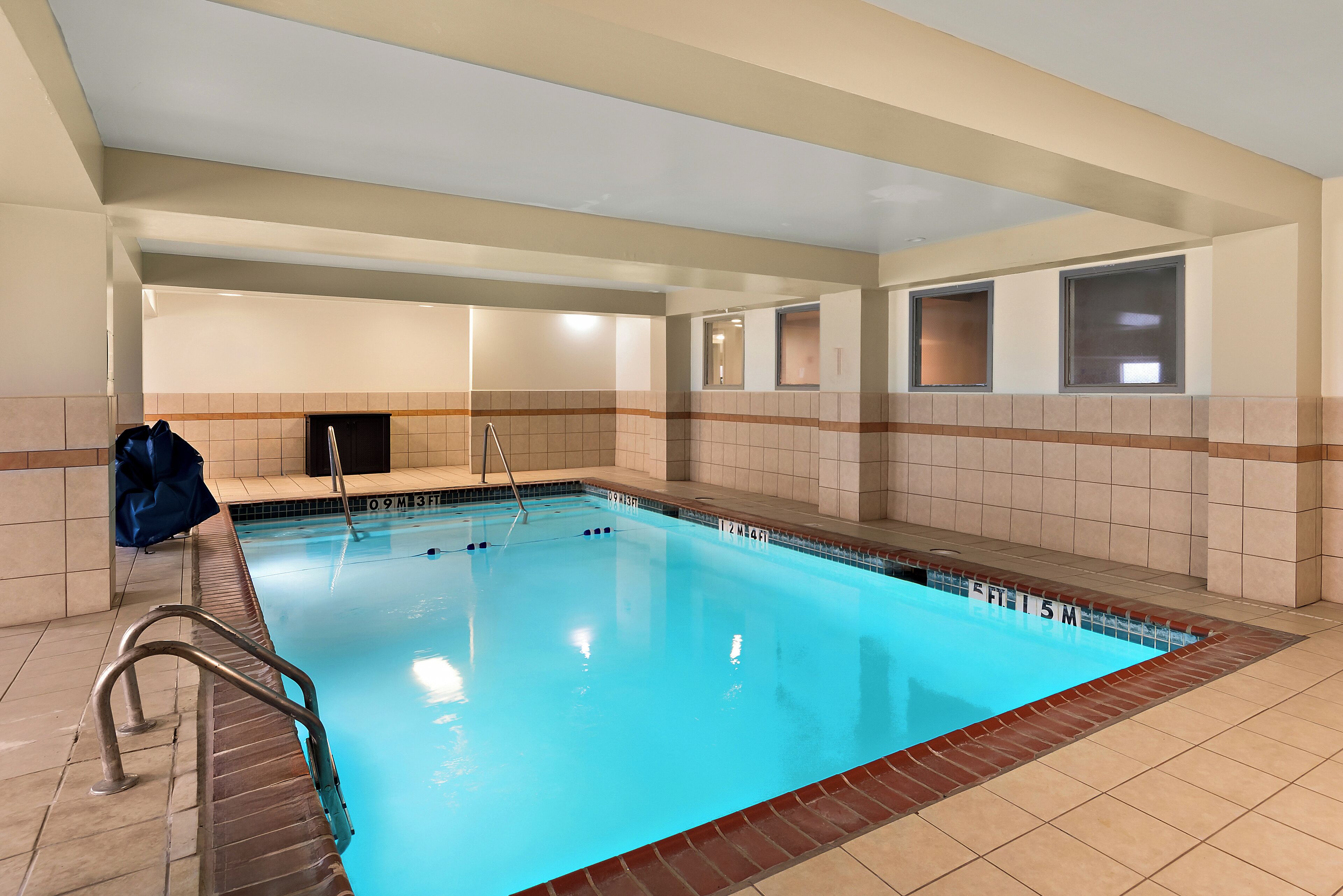 Uma grande piscina interior com marcações claras nas pistas de natação, um trampolim e chão revestido de azulejos.