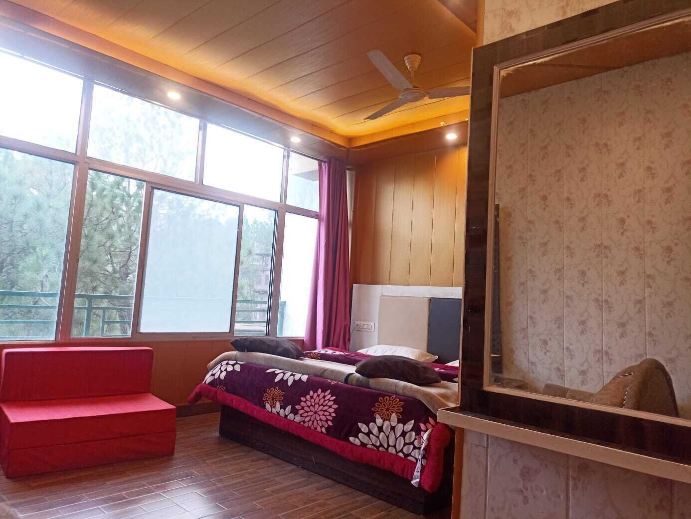 Um quarto com uma cama, uma cadeira vermelha, uma janela grande e um ventilador de teto.