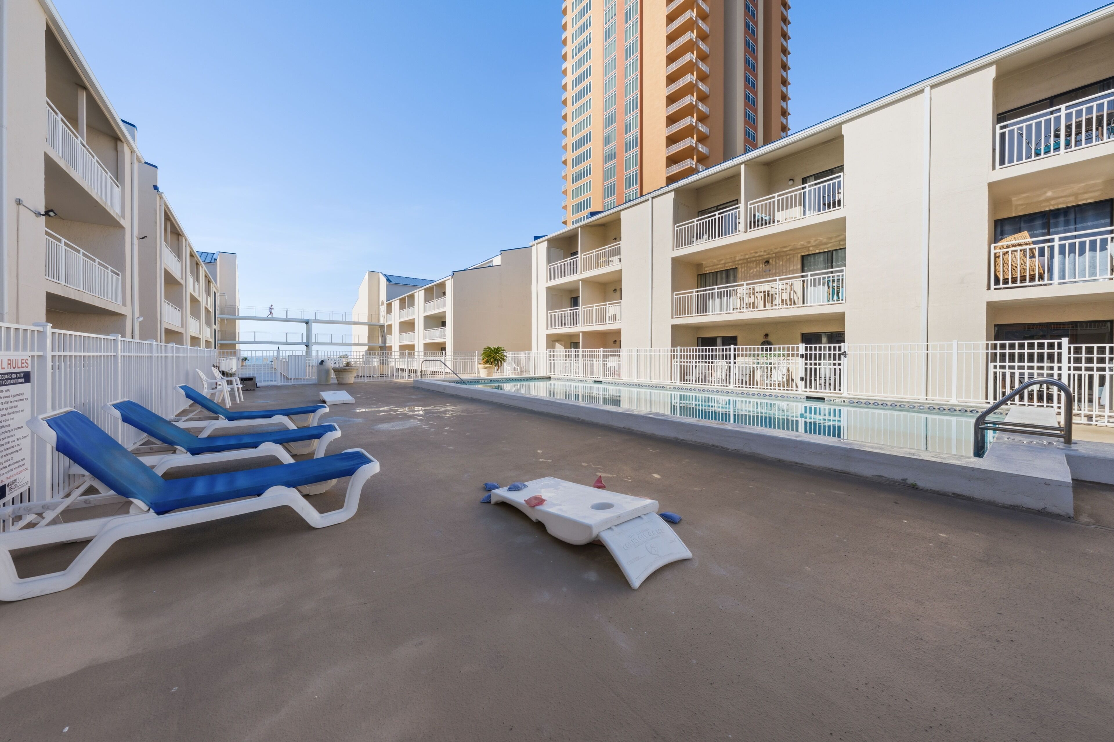 Área da piscina com espreguiçadeiras, piscina e um edifício alto ao fundo.