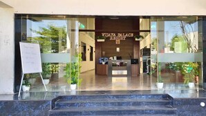 Entrada do Vijaya Palace Resort, com balcão de recepção, portas de vidro e plantas em vasos.