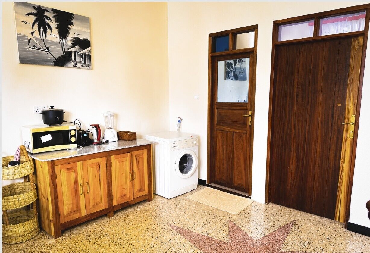 Cozinha compacta com micro-ondas, torradeira e máquina de lavar roupa, armários de madeira e um chão com padrão de estrelas.