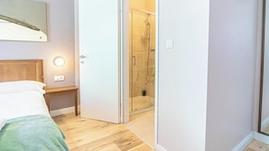 Quarto com cama, mesa de cabeceira e luminária fixada na parede.