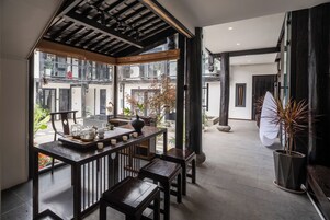 Quarto japonês tradicional com piso de tatame, uma mesa baixa com um conjunto de chá e vista para o jardim exterior.