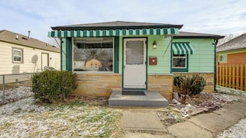 Uma casa térrea com fachada verde e branca, uma porta da frente e um pequeno alpendre com toldo verde.