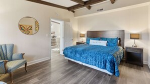 Quarto com uma cama grande, vigas de madeira no teto, um espelho redondo e uma cadeira.