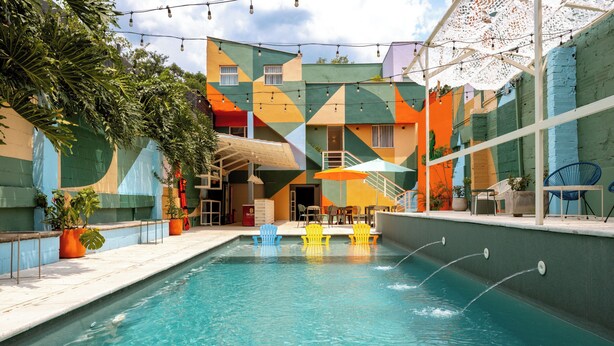 Piscina com cadeiras coloridas, área de estar coberta e um edifício com padrões geométricos.