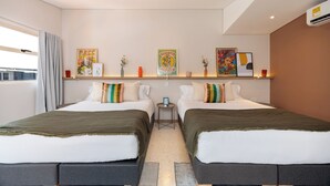 Quarto de hotel com duas camas, uma mesa pequena e obras de arte nas paredes.