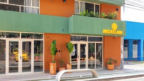 Um edifício com toldo verde, uma placa com a inscrição 'MEDELLIN' e grandes vasos de plantas.