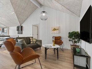 Uma sala de estar moderna com pé direito alto, uma TV de tela plana na parede, uma mesa de centro redonda e um sofá com almofadas.
