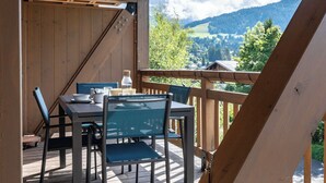 Um deck de madeira com mesa e cadeiras, com vista para uma paisagem montanhosa.