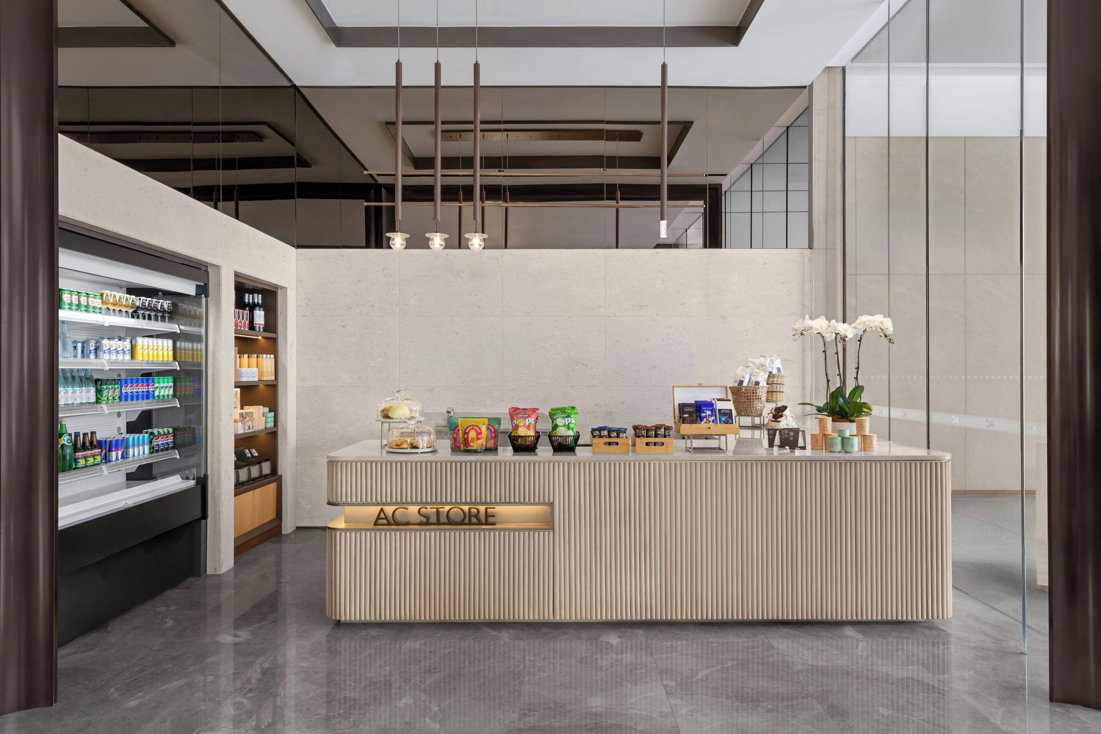 Uma loja AC moderna com design limpo e minimalista, apresentando um expositor refrigerado para bebidas e uma variedade de snacks e artigos de higiene pessoal.