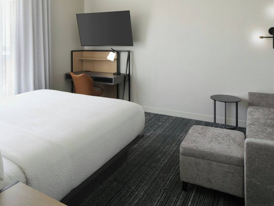 Quarto de hotel com cama, escrivaninha, cadeira, televisão e uma pequena mesa.