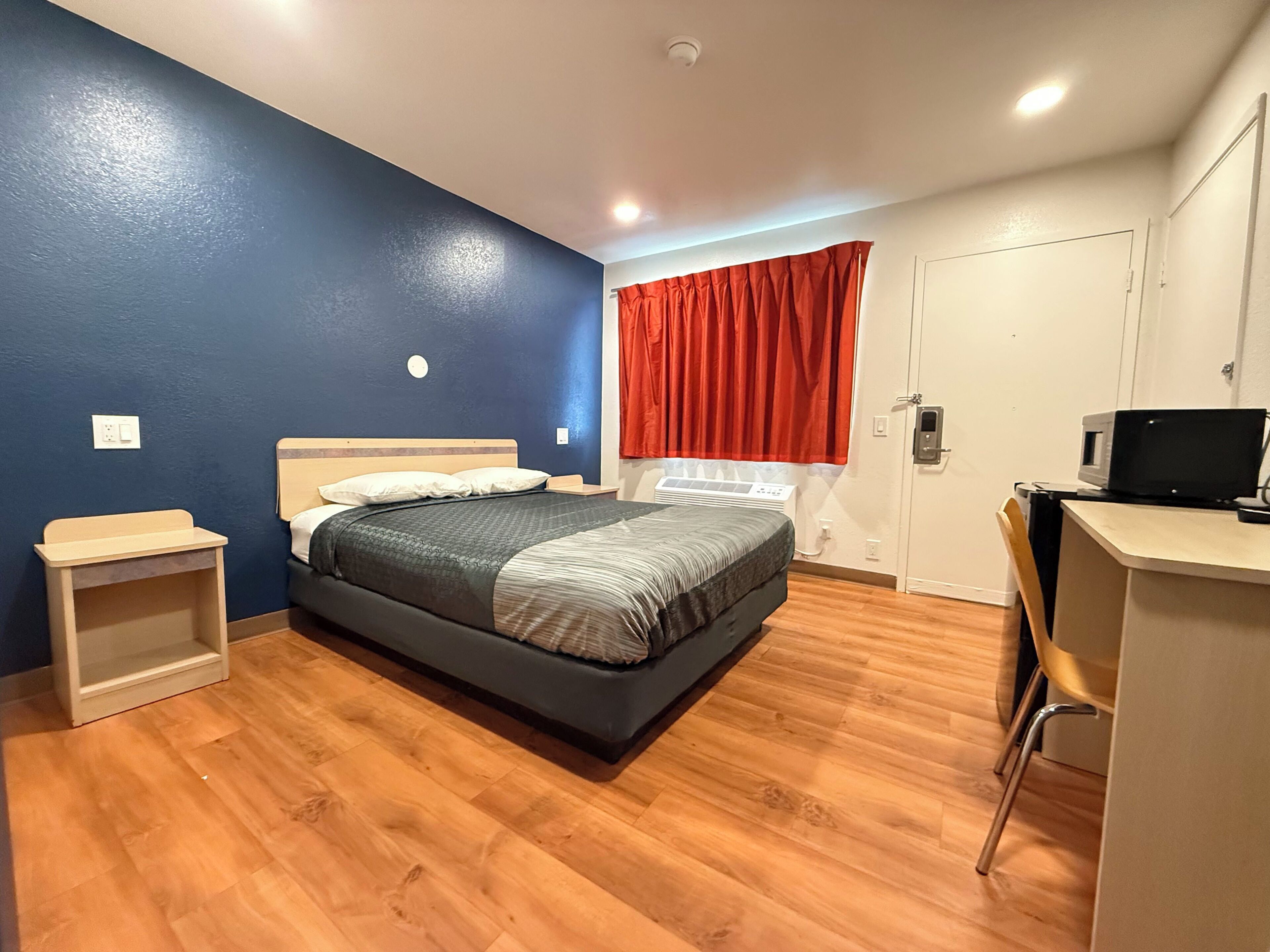 Um quarto com cama, mesas de cabeceira, escrivaninha e uma cadeira.