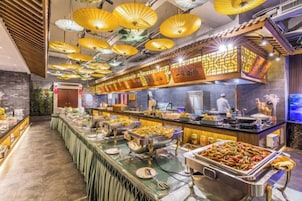 Uma área de buffet com um balcão comprido, diversas estações de comida e iluminação pendente.